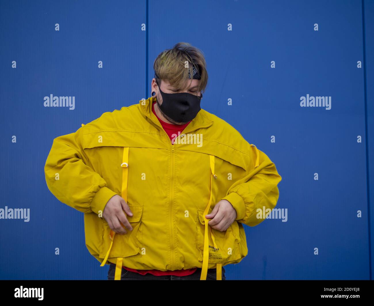 Male wearing a yellow jacket and a mask and posing by a blue wall Stock ...