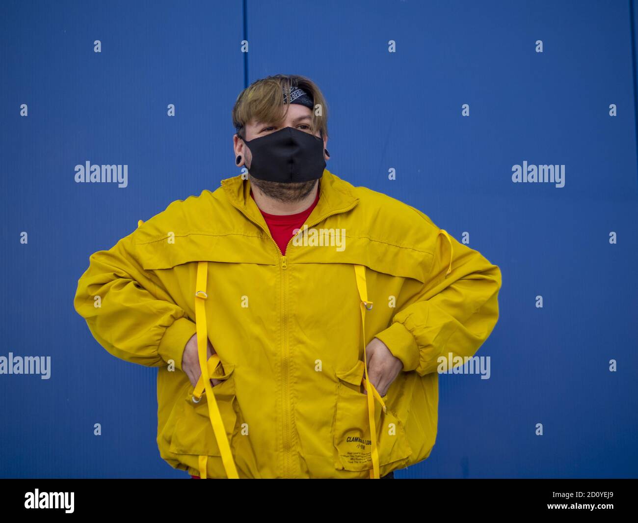 Male wearing a yellow jacket and a mask and posing by a blue wall Stock ...
