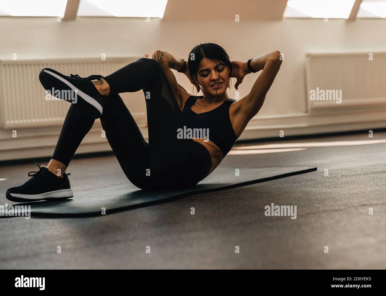 Female athlete with hands behind head doing abdominal exercise on mat ...