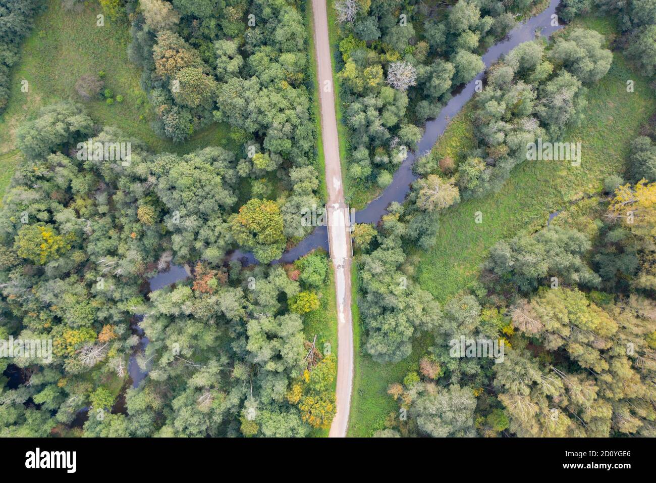 Aerial top down view of gravel road and bridge over winding river flowing through green forest ...