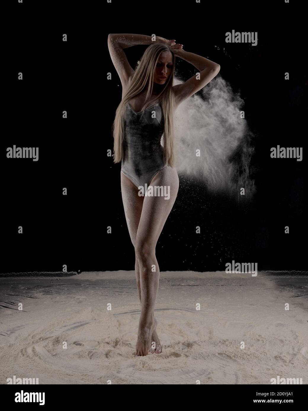 Beautiful sensual fit slim dancer in black body with long blond hair throwing dust, flour ...