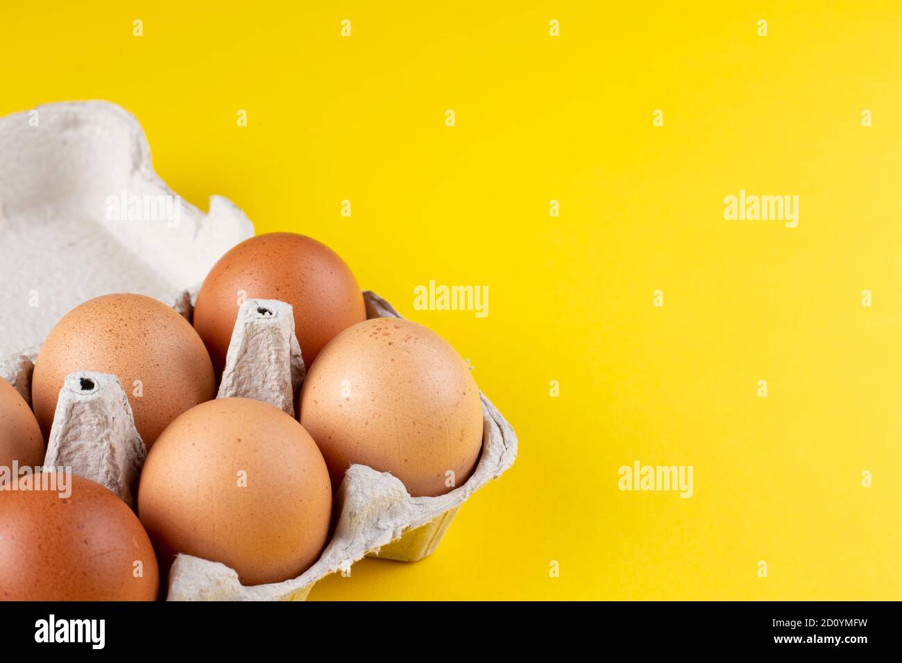 Chicken eggs in an open egg carton isolated on yellow. Top view with ...