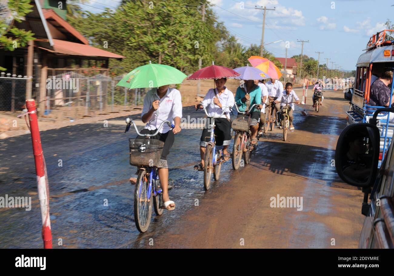 Champasak: Lao people biking with an umbrella in one hand as a sun ...
