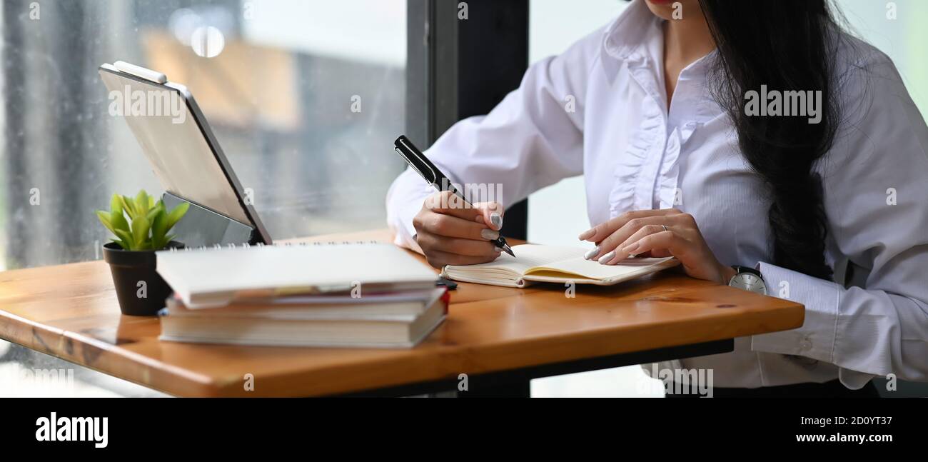 Cropped image of woman taking note on notebook paper with pen on office ...