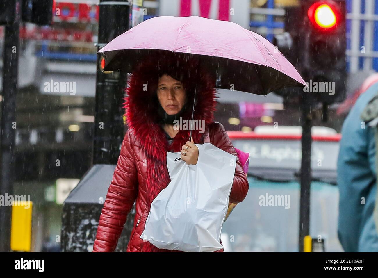 London, UK. 2nd Oct, 2020. A shopper shelters from the rain underneath ...