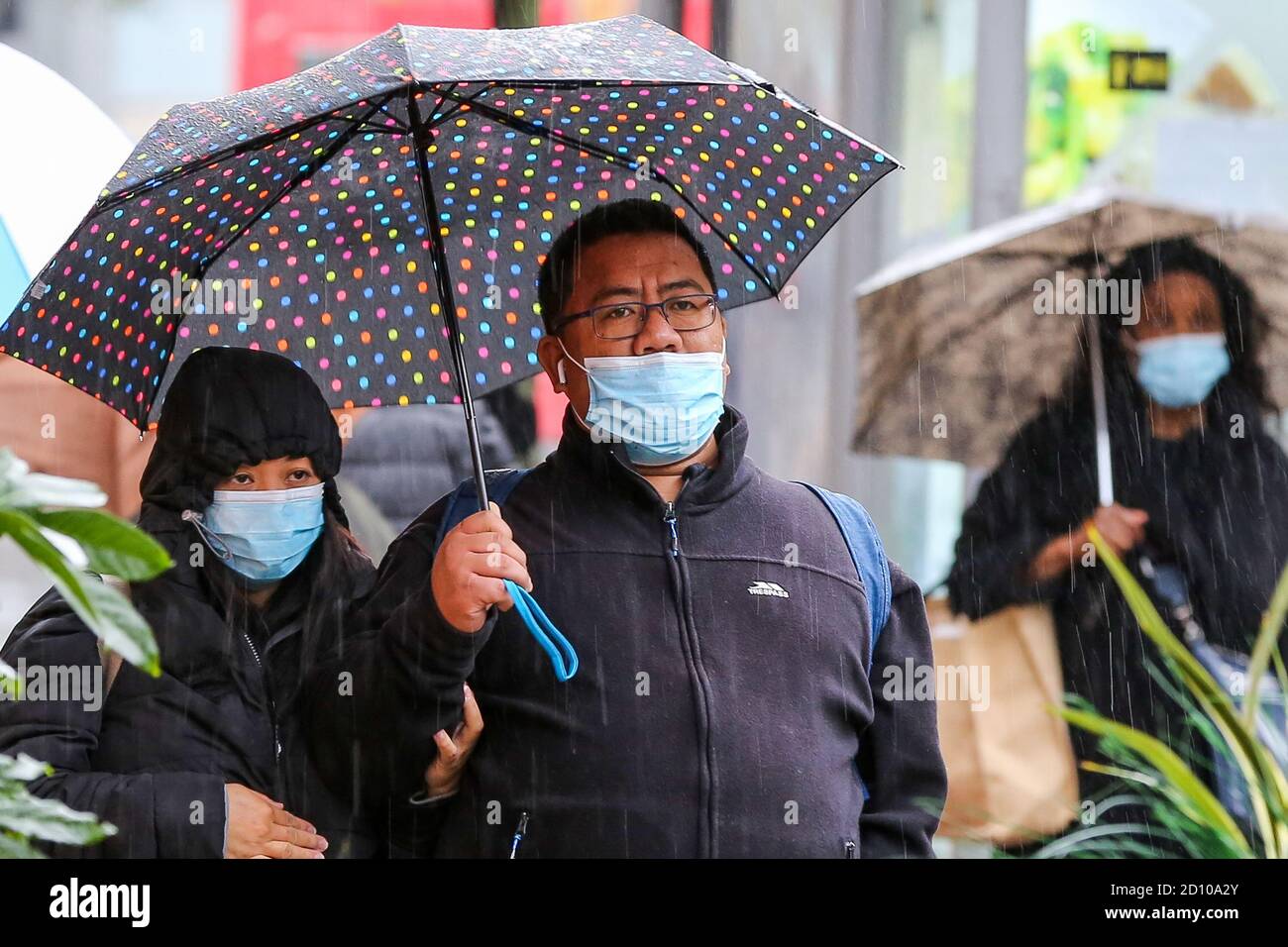 A couple wearing face masks shelter from the rain underneath an ...