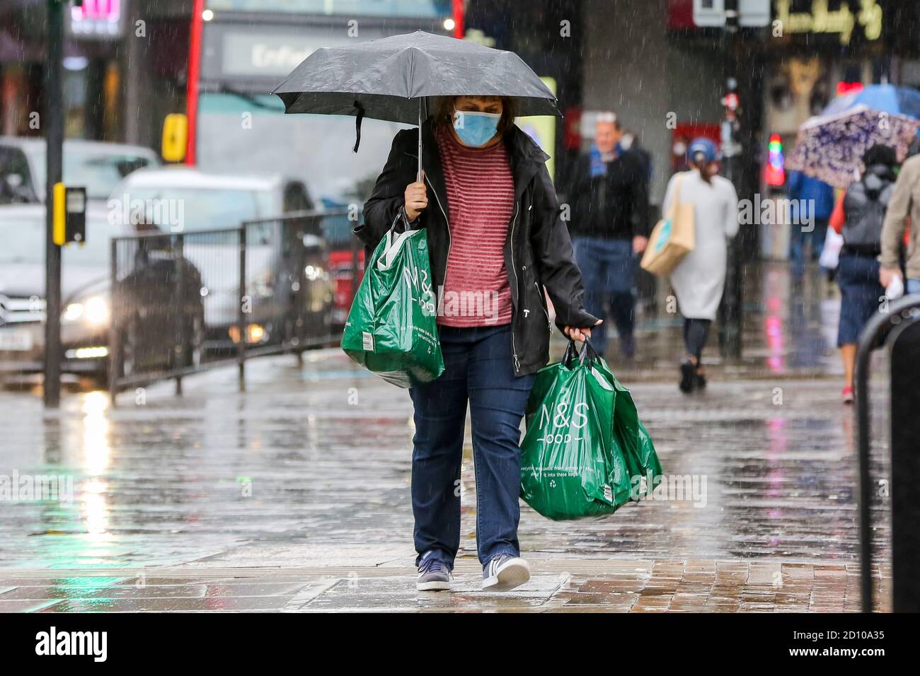 A shopper wearing a face mask shelters from the rain underneath an ...