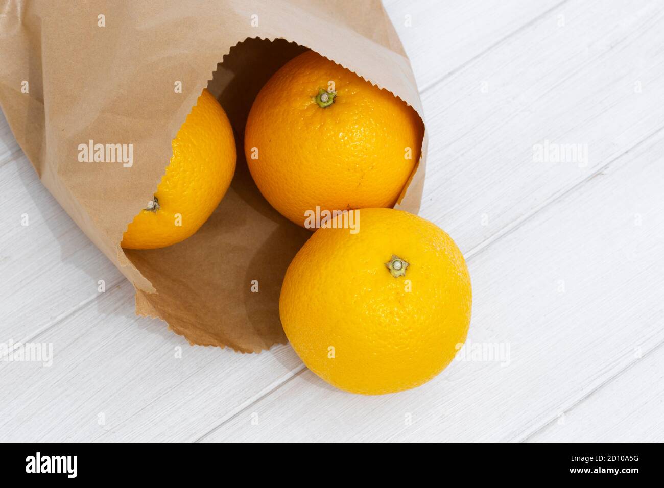 Oranges in a brown paper bag on a white wood background ...