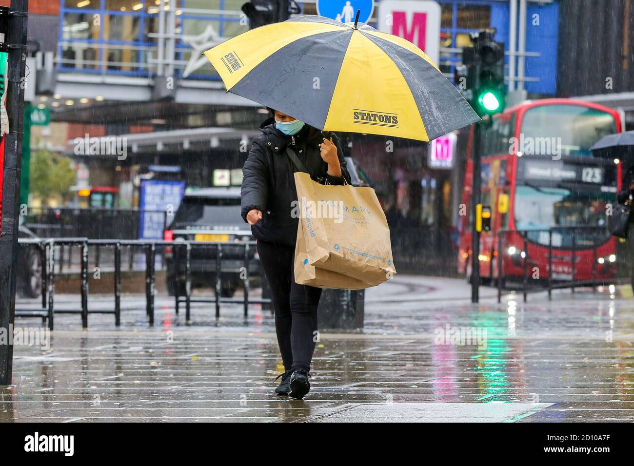 A shopper wearing a face mask shelters from the rain underneath an ...
