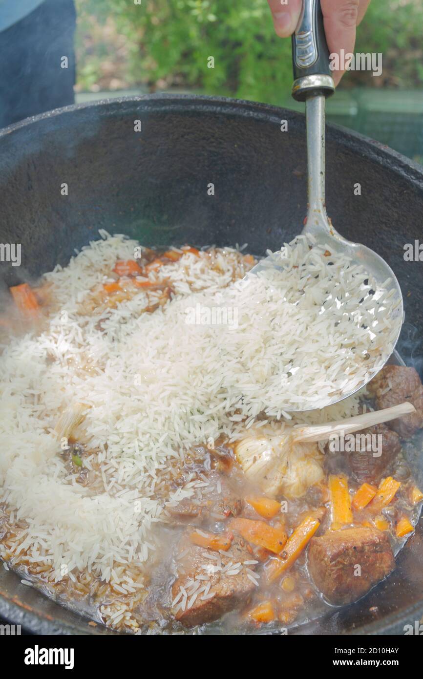 Cooking pilaf in a cauldron on the grill outside in the summer Stock ...