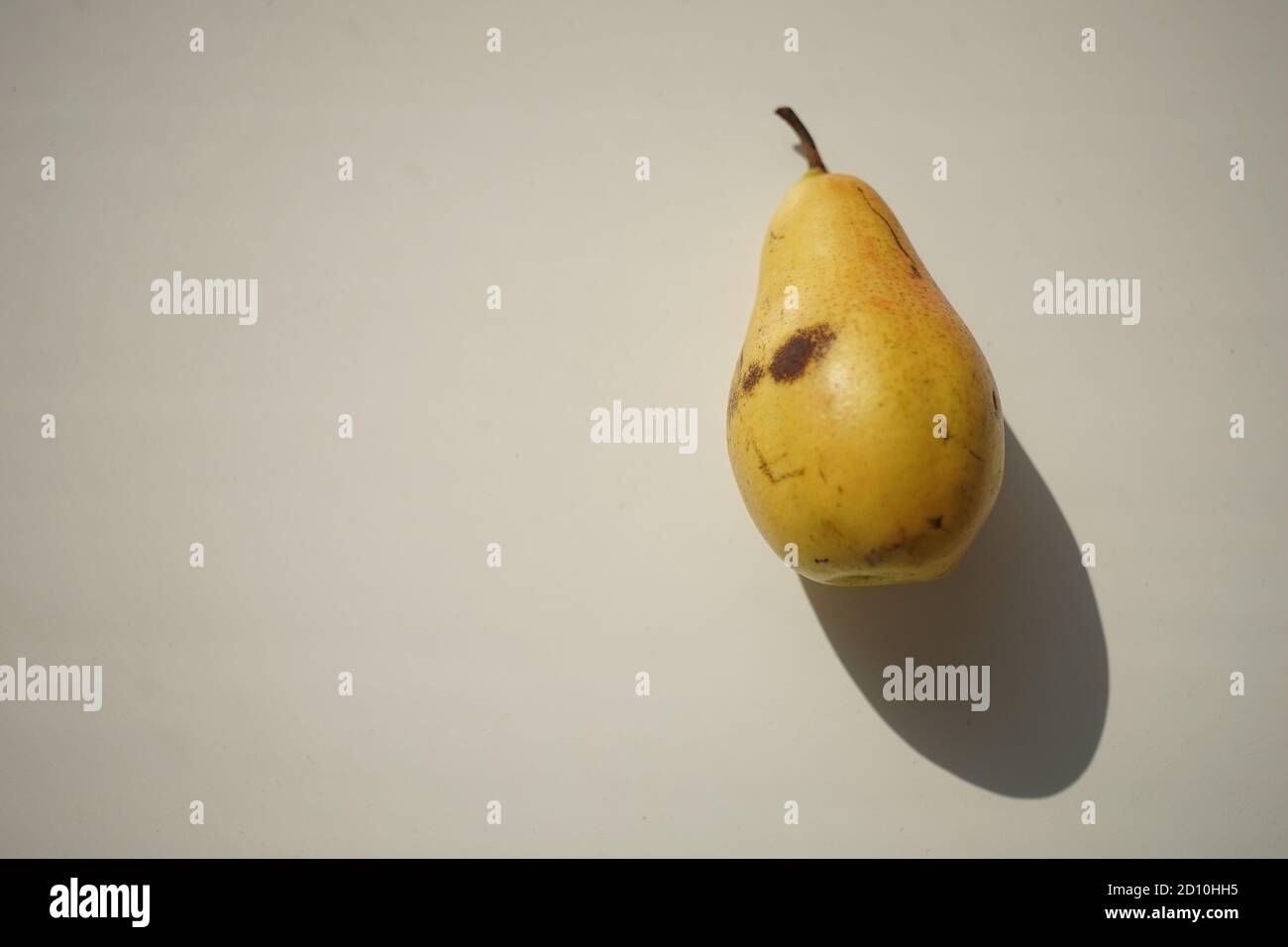 One shabby yellow pear on a white sunny table with strong shadow Stock ...