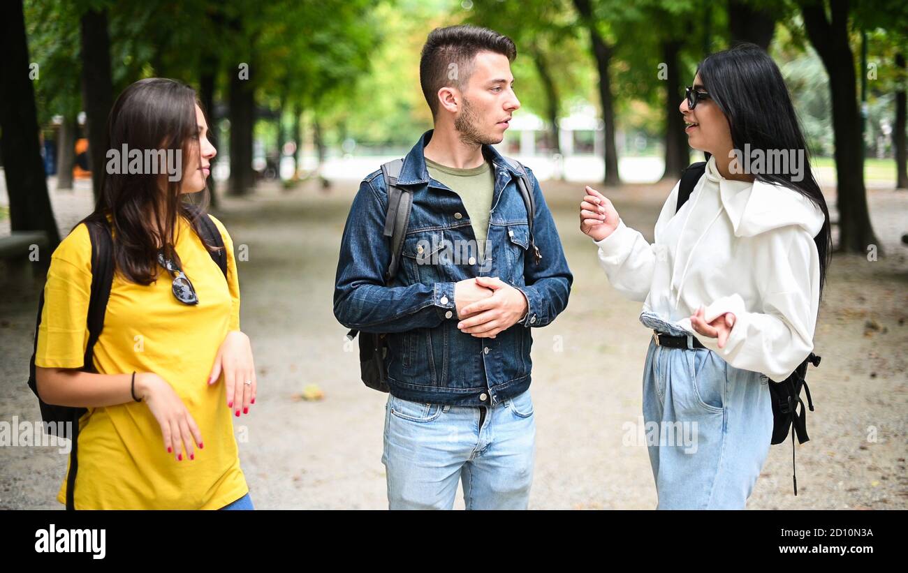 Three students talking to each other outdoor in a college courtyard ...