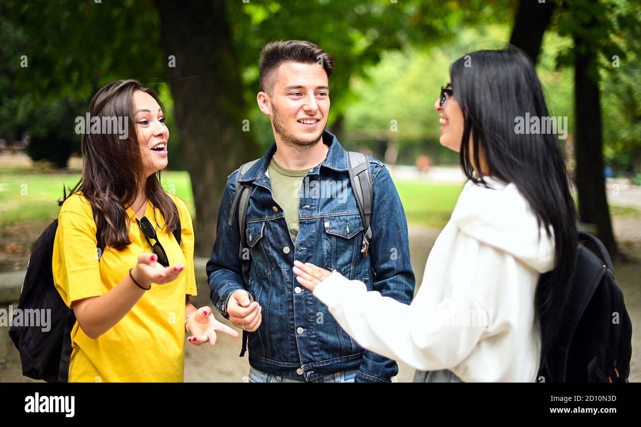 Three students talking to each other outdoor in a college courtyard ...