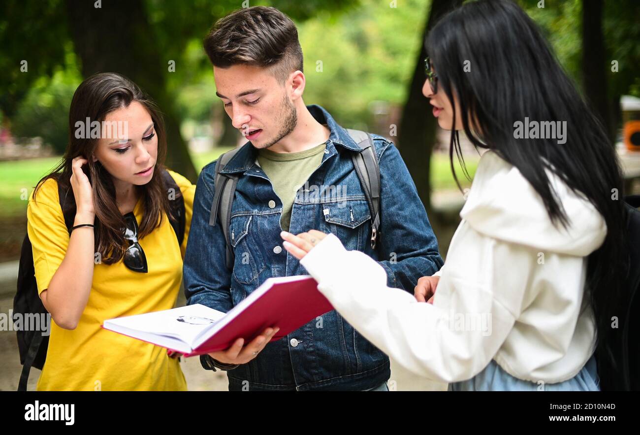 Three students talking to each other outdoor in a college courtyard ...