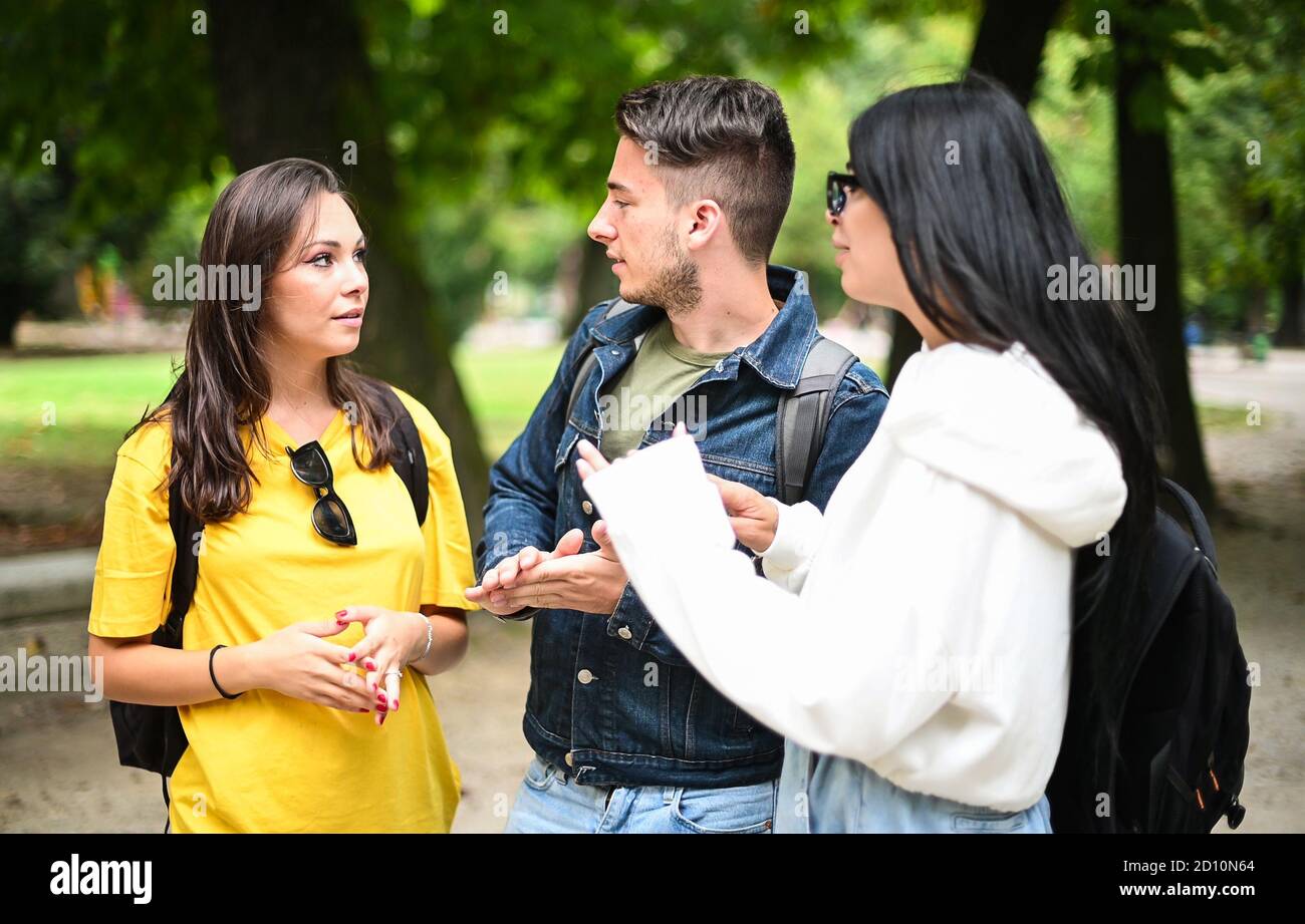 Three students talking to each other outdoor in a college courtyard ...
