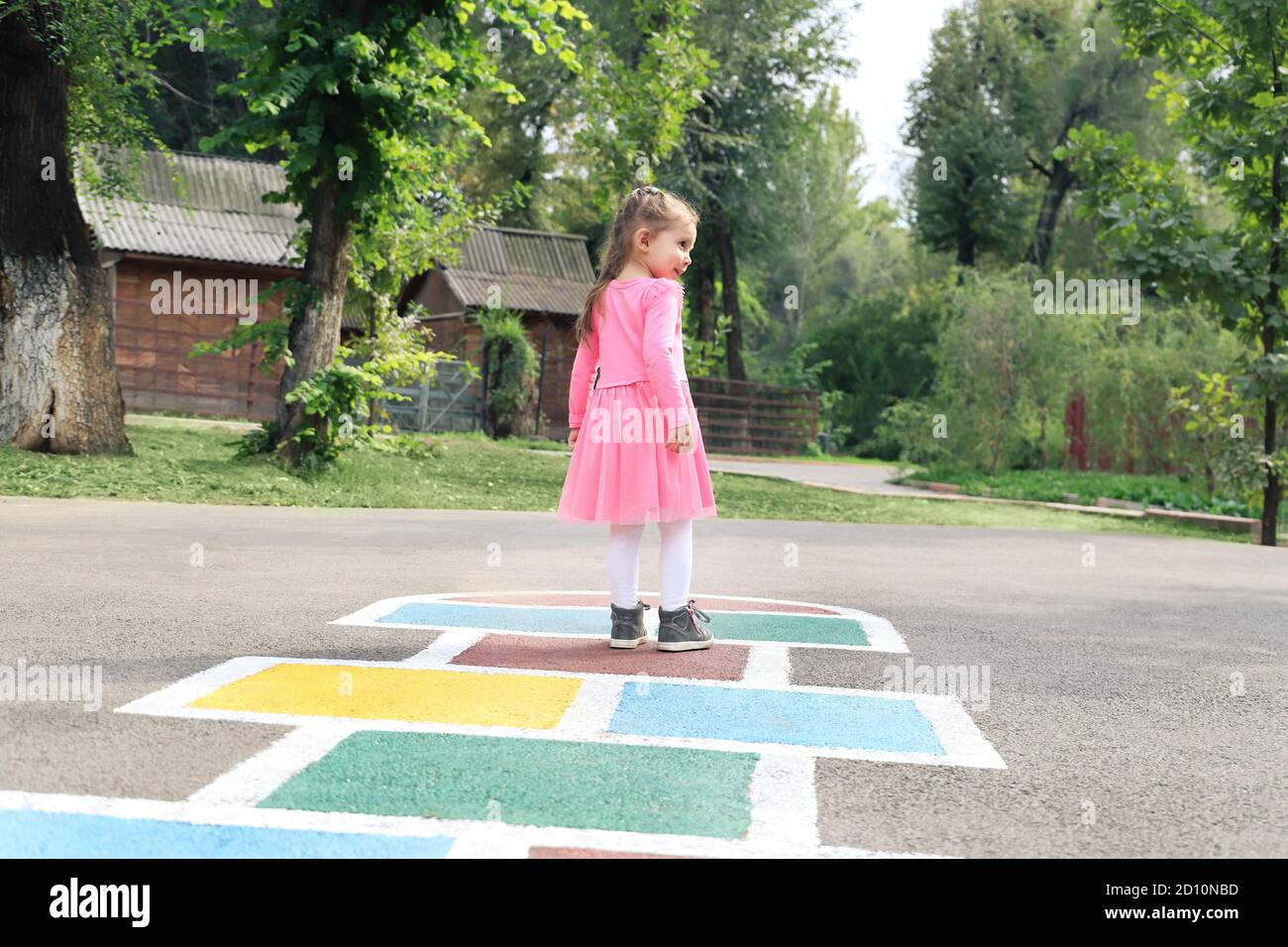 Little girl in a pink dress playing hopscotch on playground outdoors ...