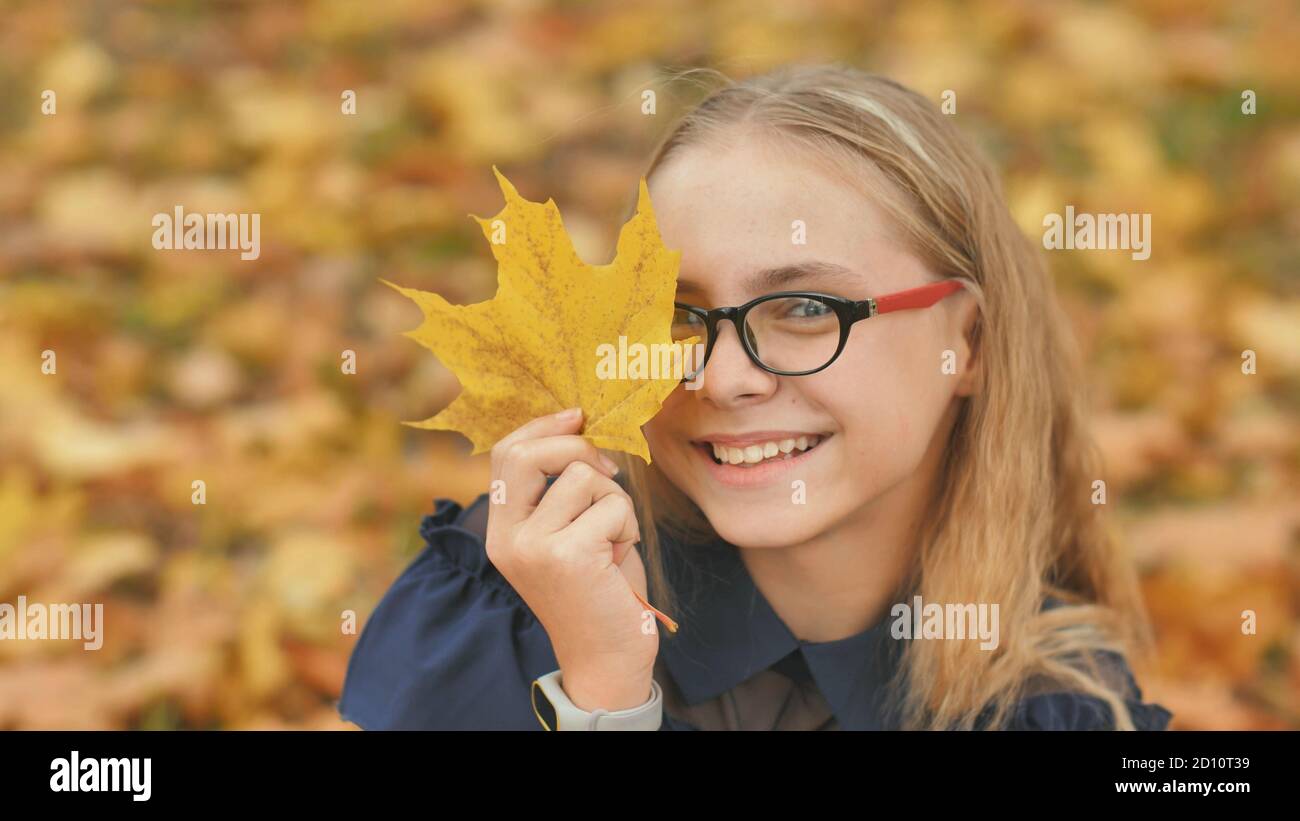 A young girl of 13 years old with autumn leaves poses in front of a ...