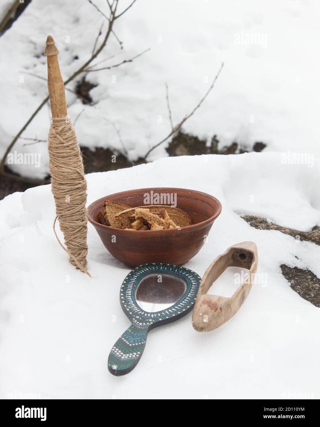 Spindle, mirror and clay plate with bread in the snow. Pagan altar ...