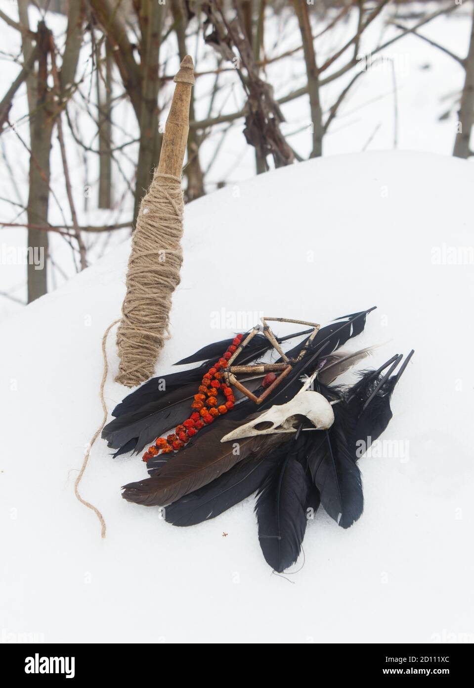 Spindle, crow feathers, bird skull and rowan beads in the snow. Still ...