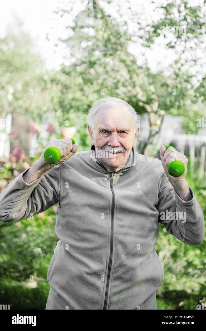 old man trains his muscles with dumbbells in the Park after a home ...