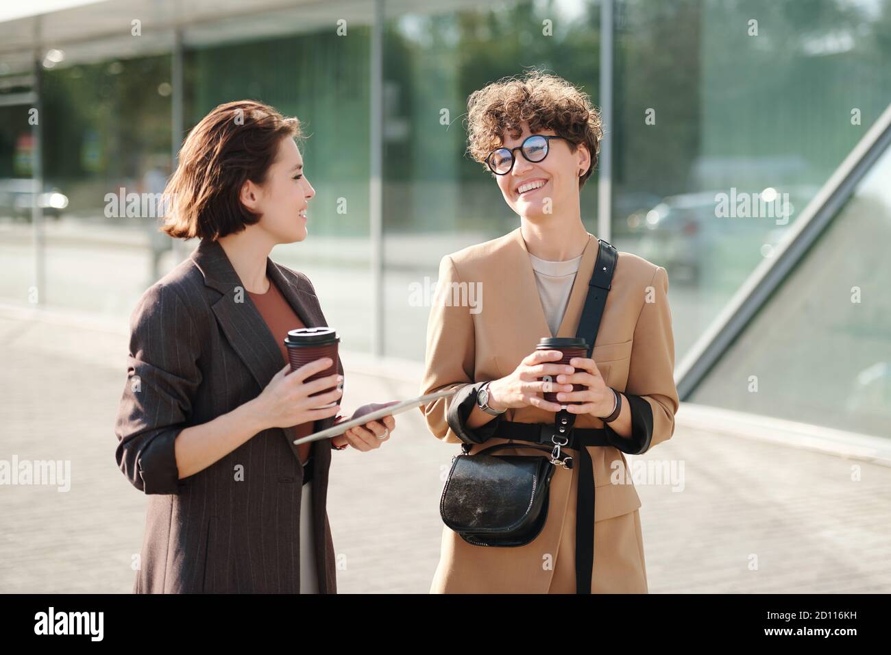 Cheerful female colleagues with drinks talking and laughing in urban ...