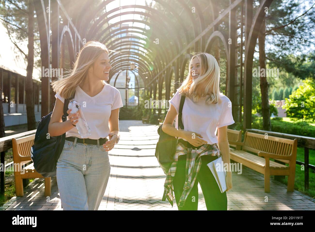 Two happy smiling talking girls teenagers students walking together ...