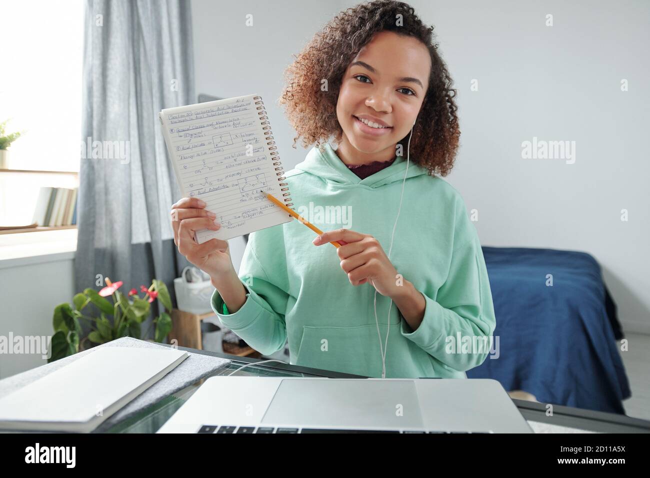 Cheerful student pointing at notes in copybook and explaining them to ...