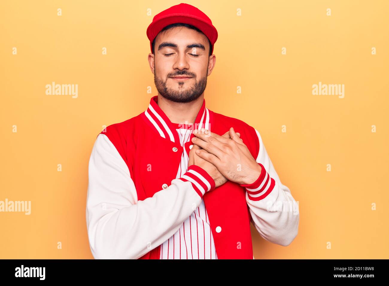 Handsome sporty man with beard wearing baseball jacket and cap over ...