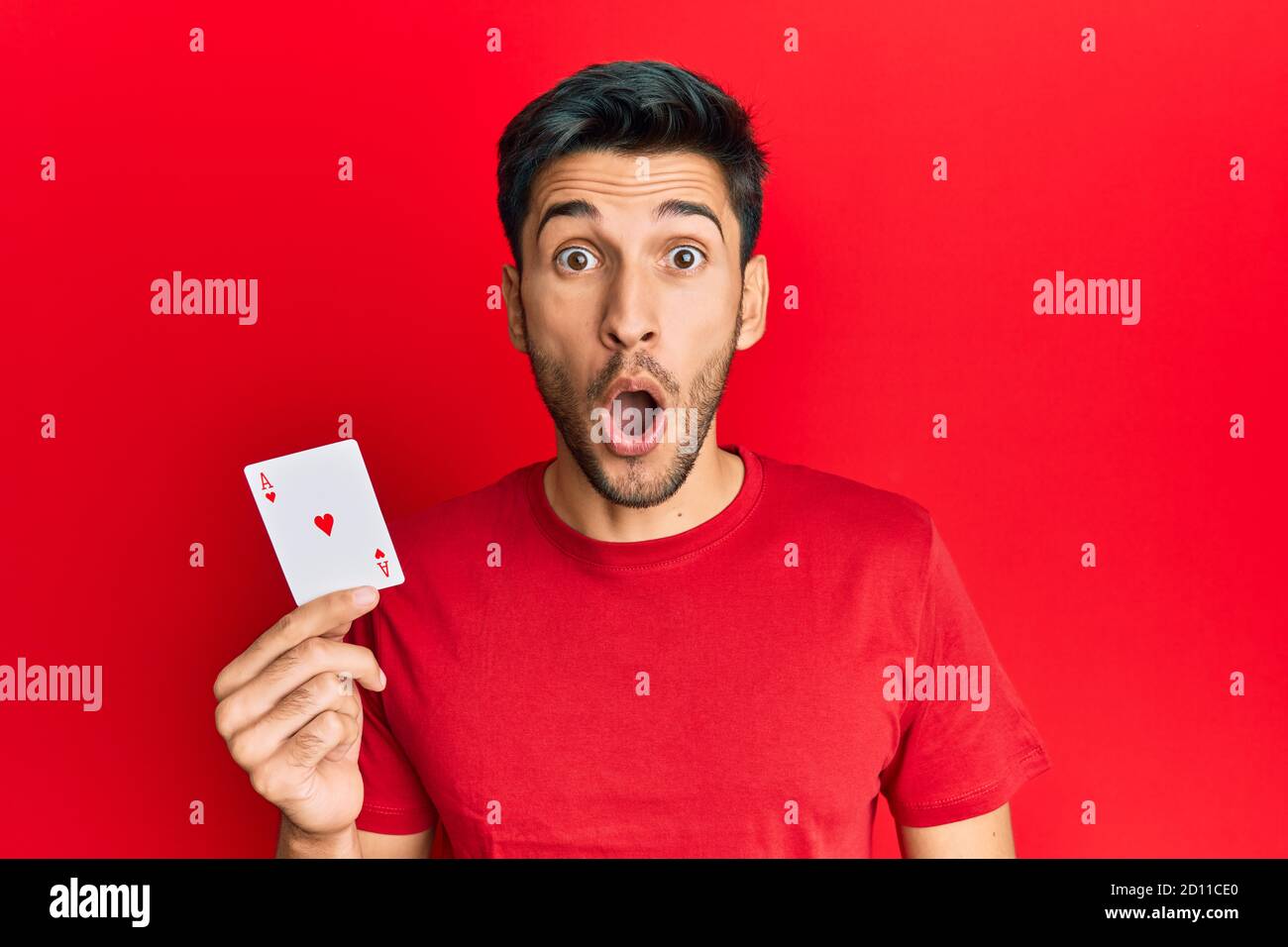 Young handsome man holding ace poker card scared and amazed with open ...