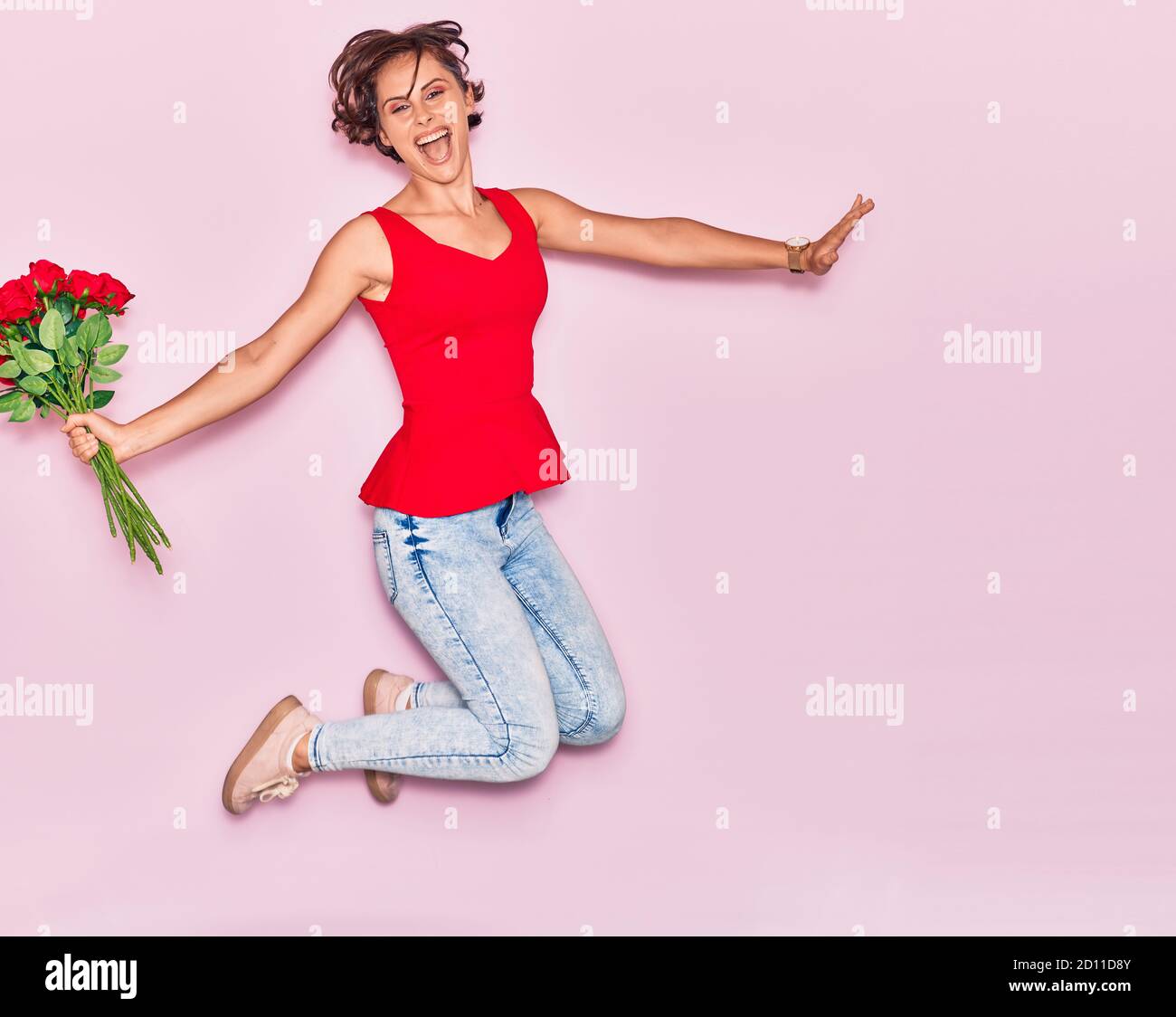 Young beautiful woman holding bouquet of roses smiling happy. Jumping ...