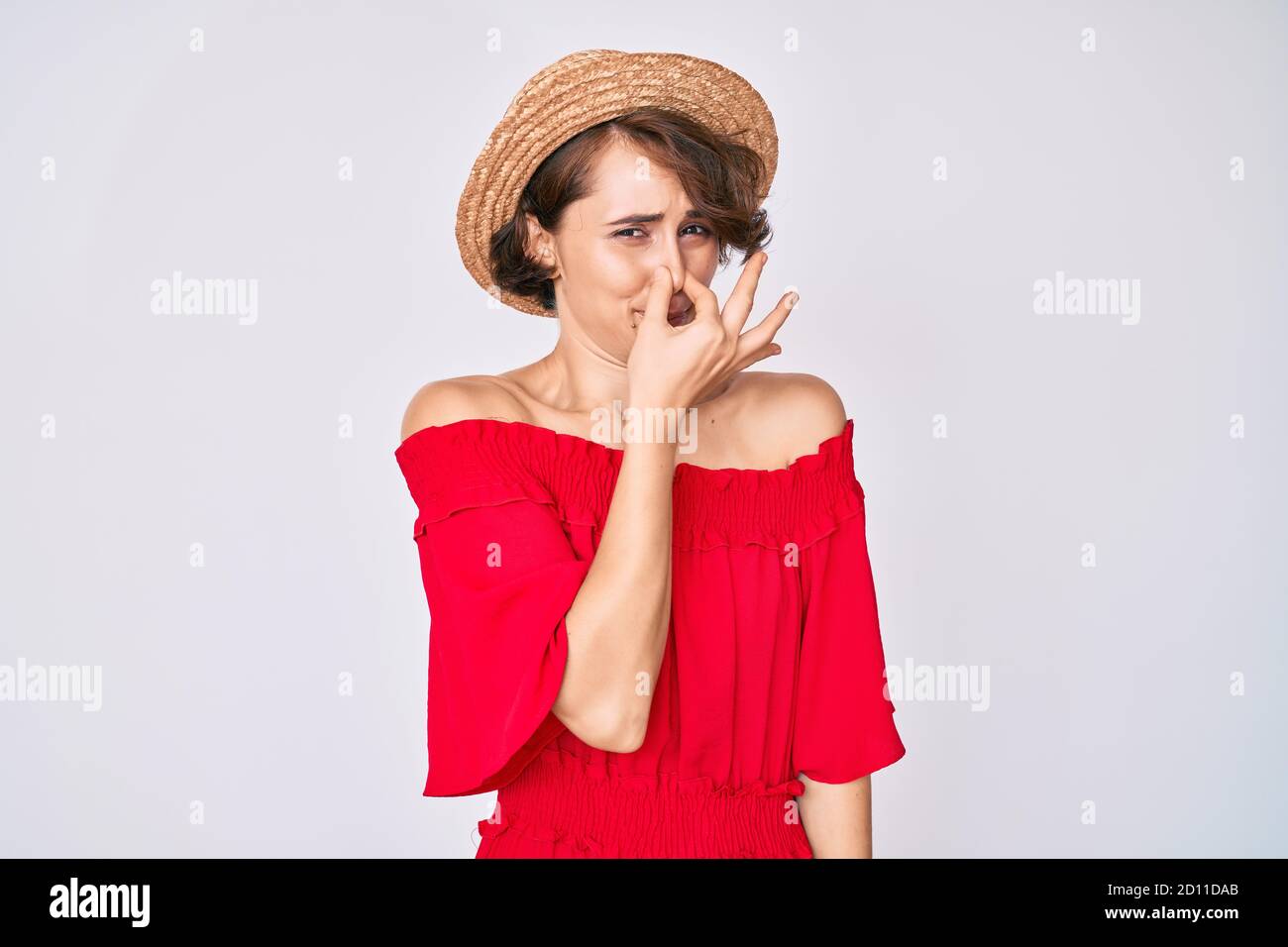 Young hispanic woman wearing summer hat smelling something stinky and ...