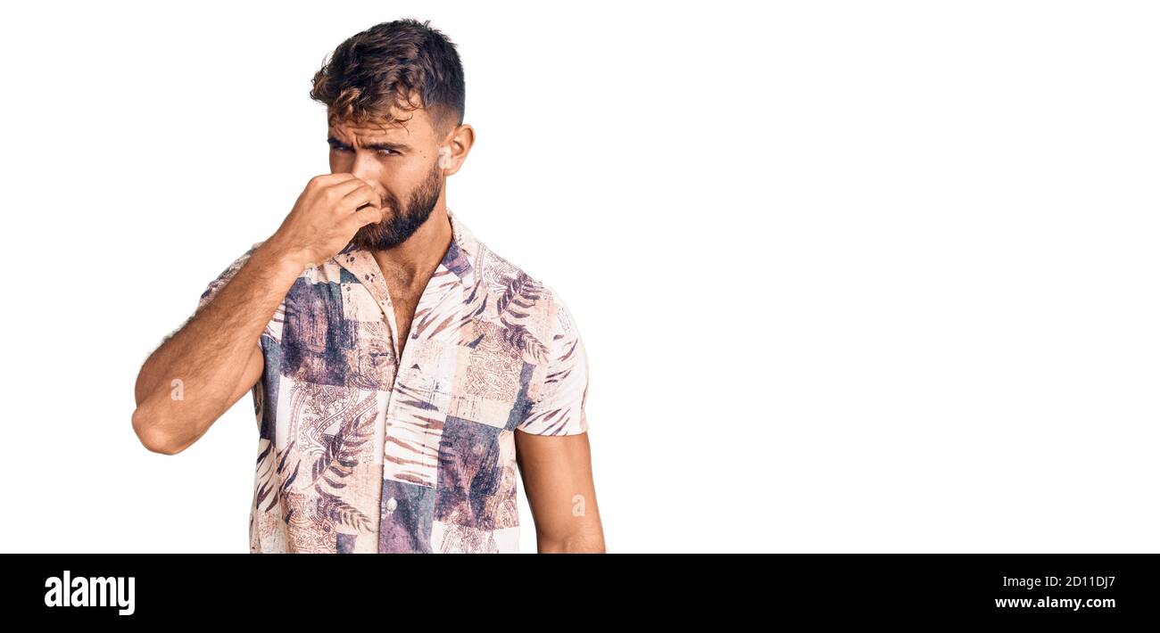 Young hispanic man wearing summer clothes smelling something stinky and ...