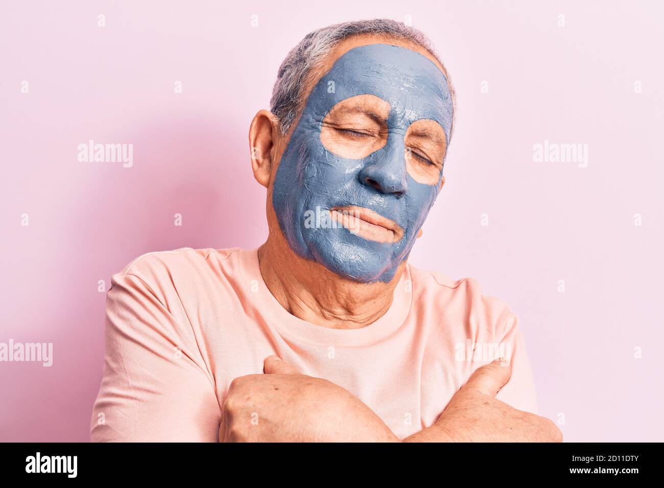 Senior man with grey hair wearing mud mask hugging oneself happy and ...