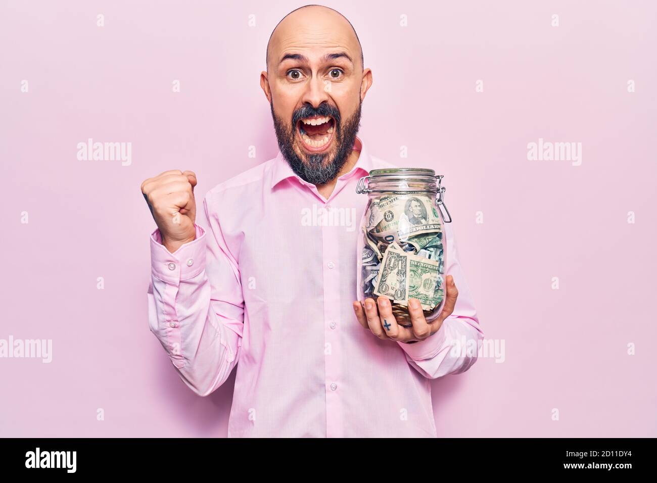 Young handsome man holding jar with savings screaming proud ...