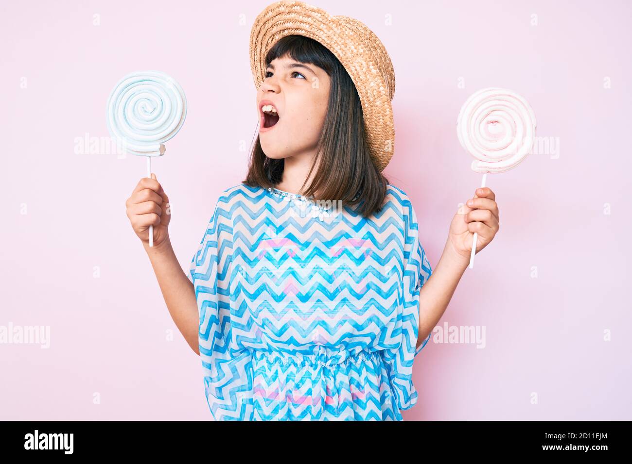 Young little girl with bang wearing summer dress eating candy angry and ...