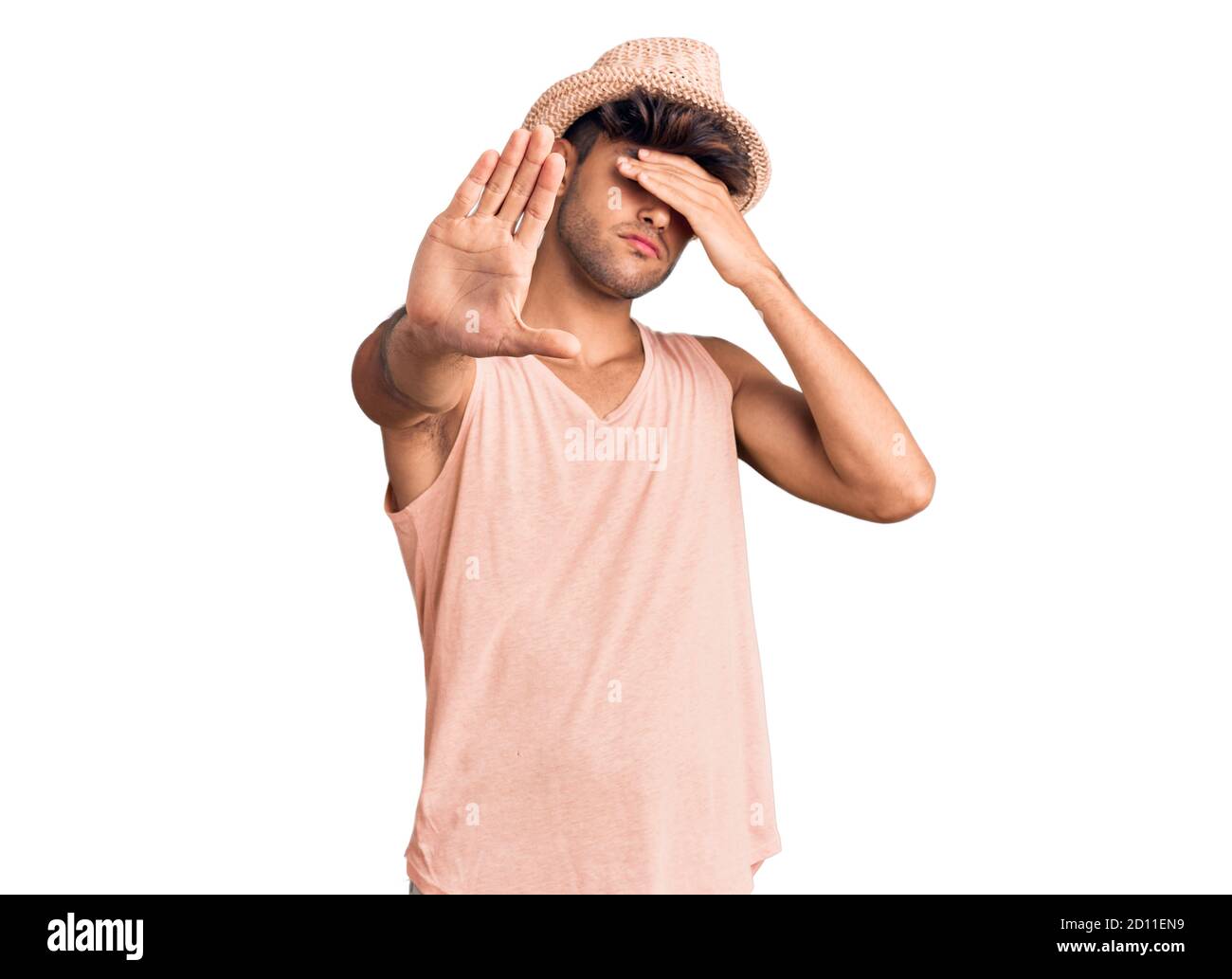 Young hispanic man wearing summer hat covering eyes with hands and ...