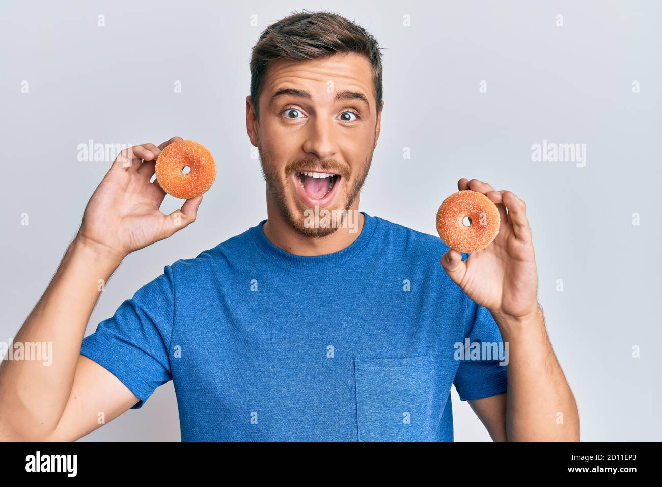 Handsome caucasian man eating donuts celebrating crazy and amazed for ...