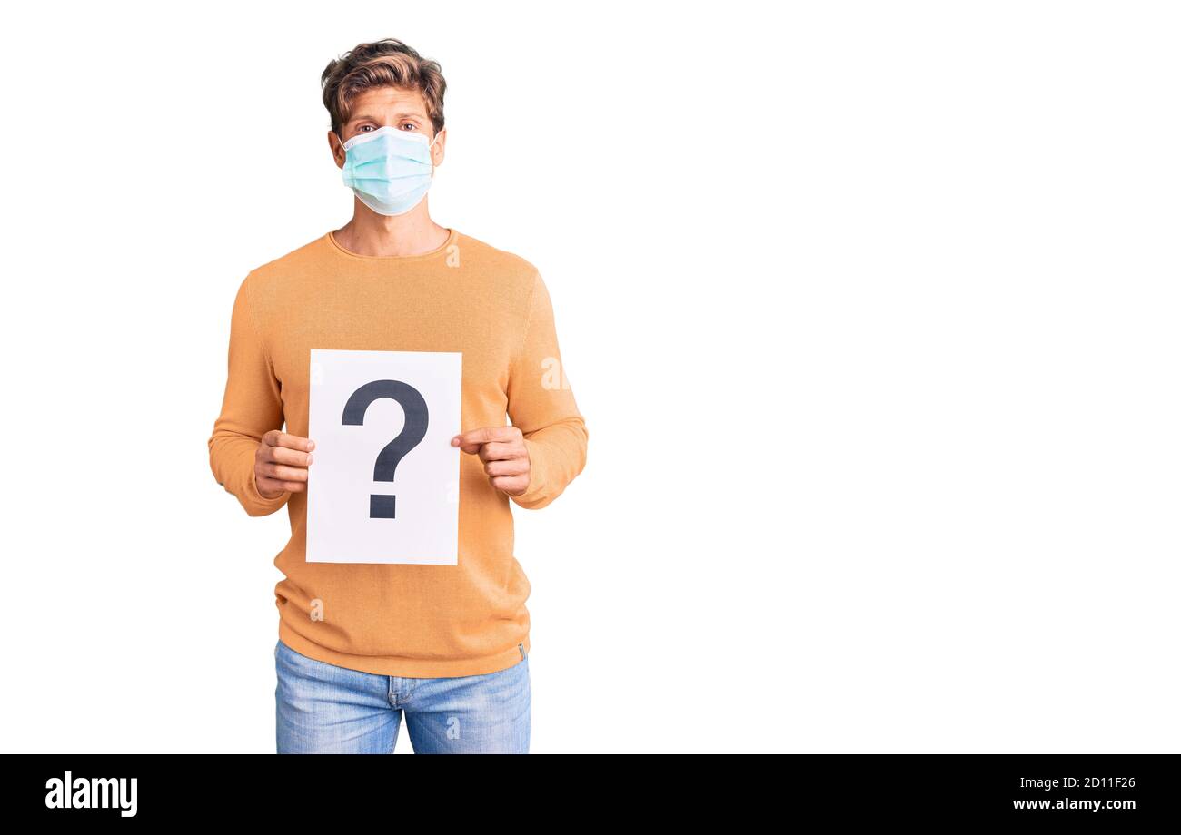 Young handsome man wearing medical mask holding question mark looking ...
