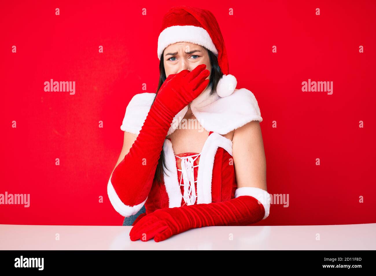 Young caucasian woman wearing santa claus costume smelling something ...