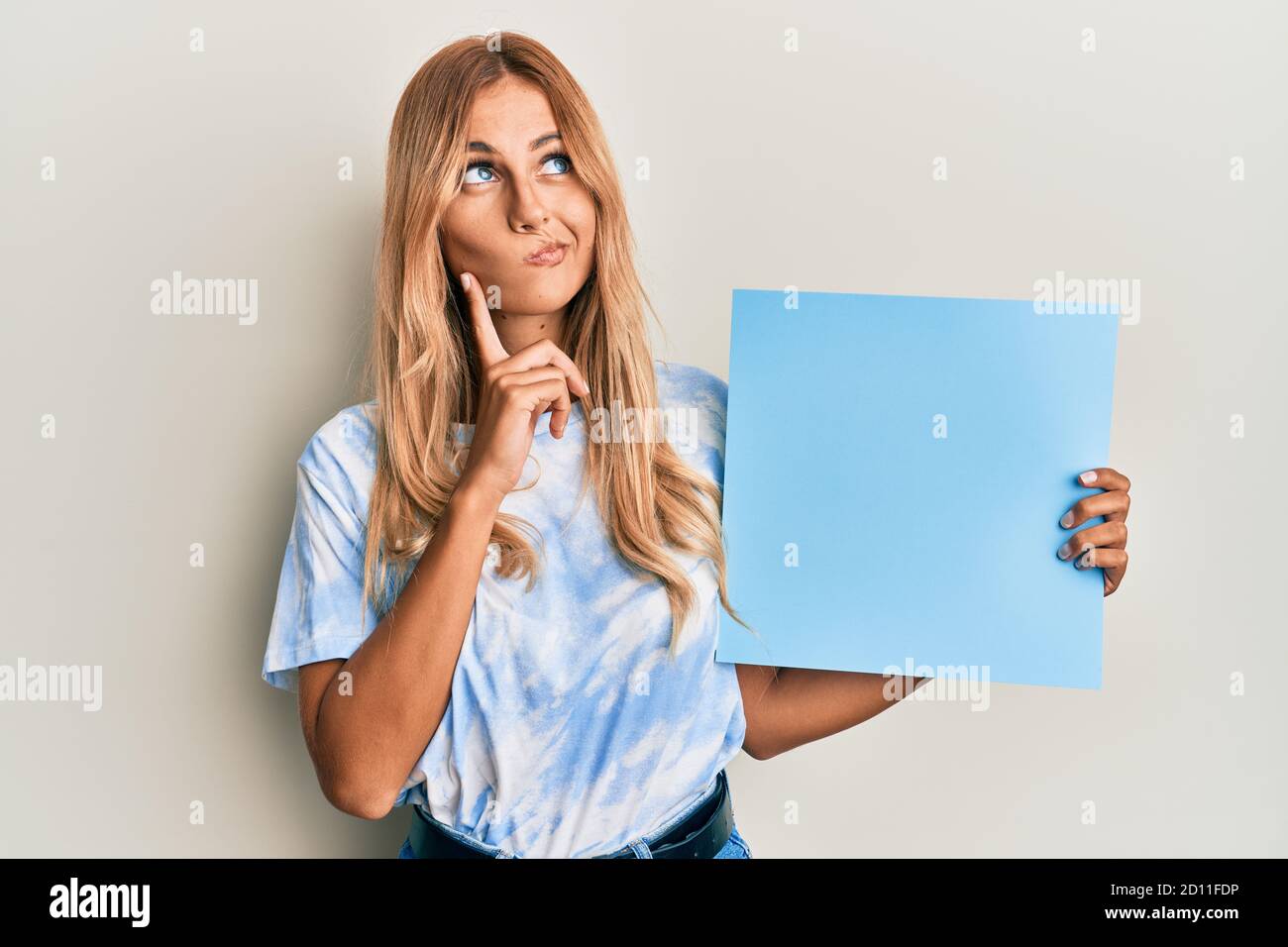 Beautiful blonde young woman holding blank empty blue banner serious ...