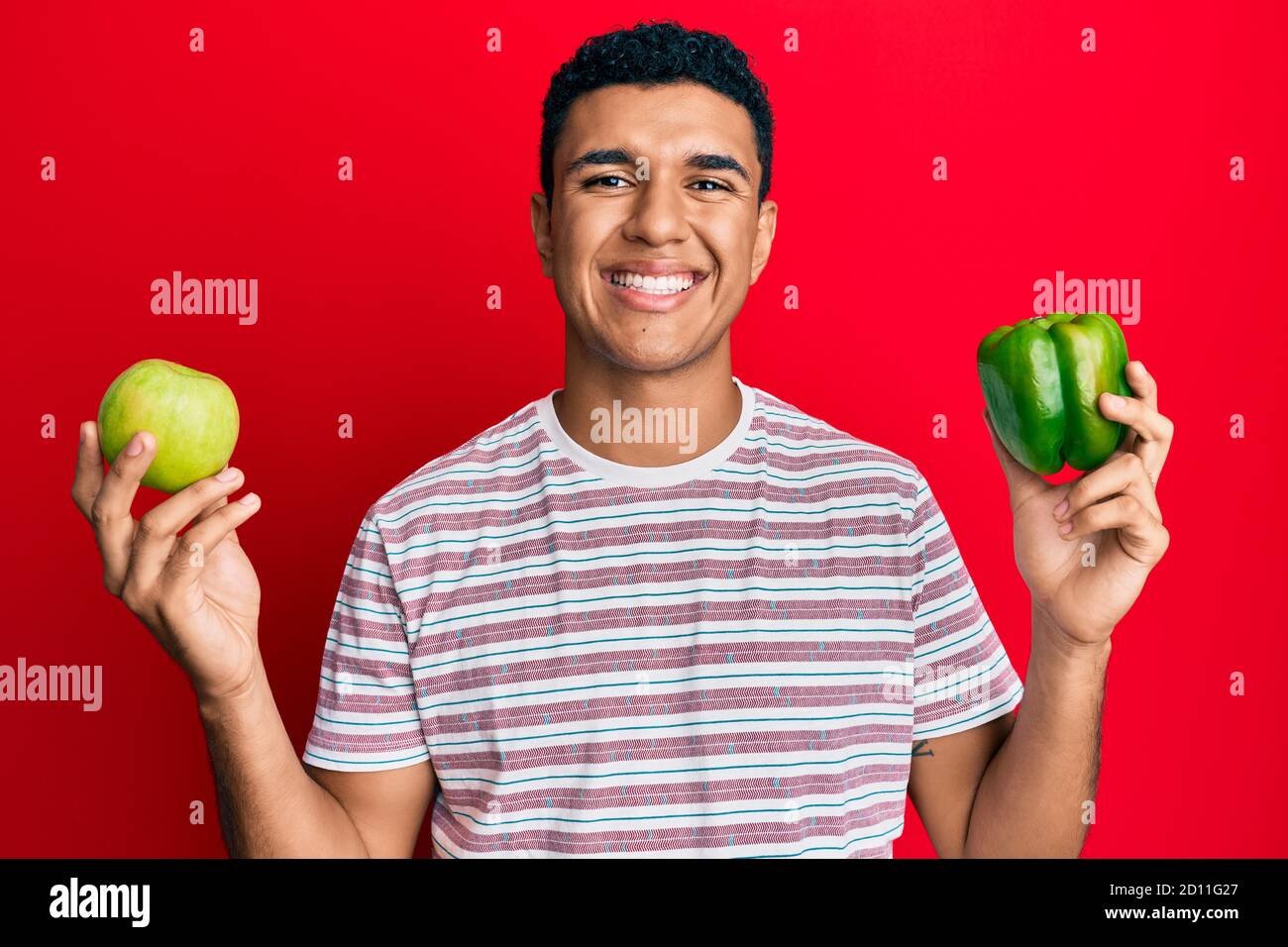 Young arab man holding green apple and pepper smiling with a happy and ...