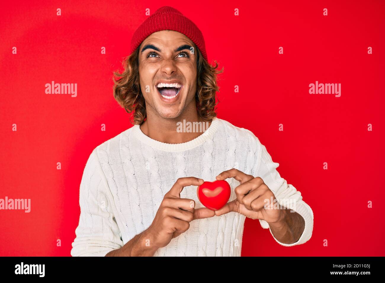 Young hispanic man holding heart angry and mad screaming frustrated and ...