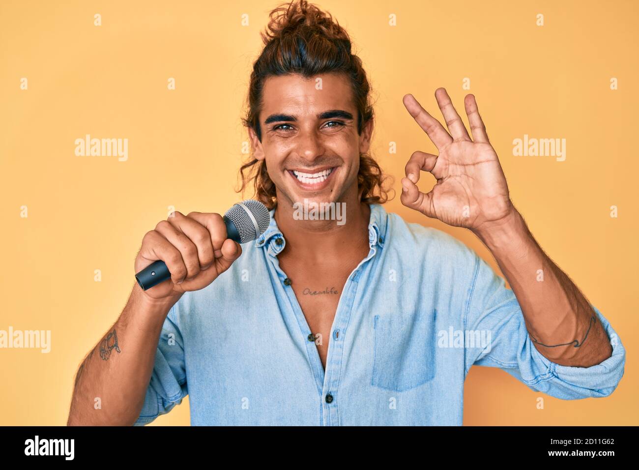 Young hispanic man singing song using microphone doing ok sign with ...
