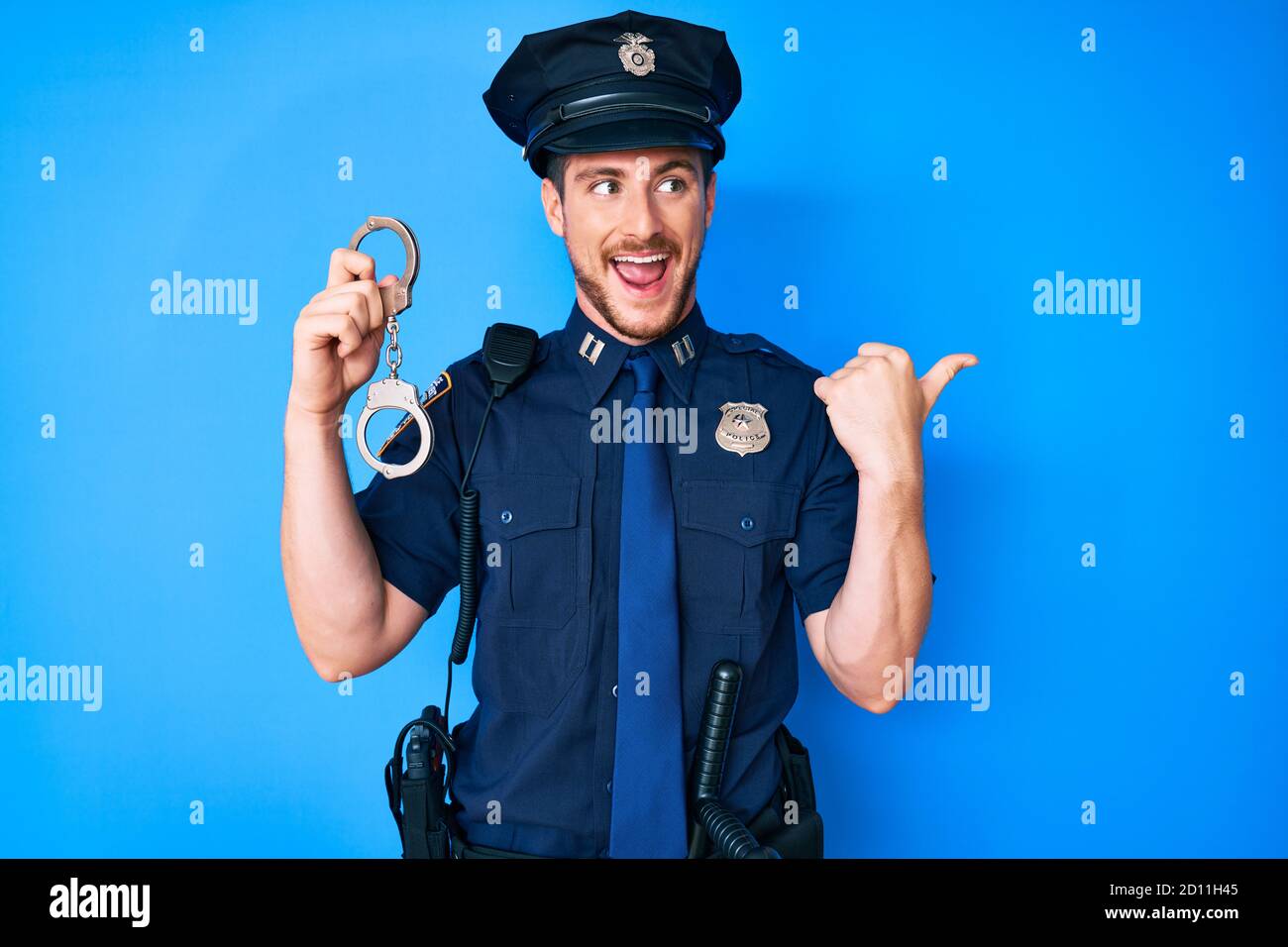 Young caucasian man wearing police uniform holding handcuffs pointing ...