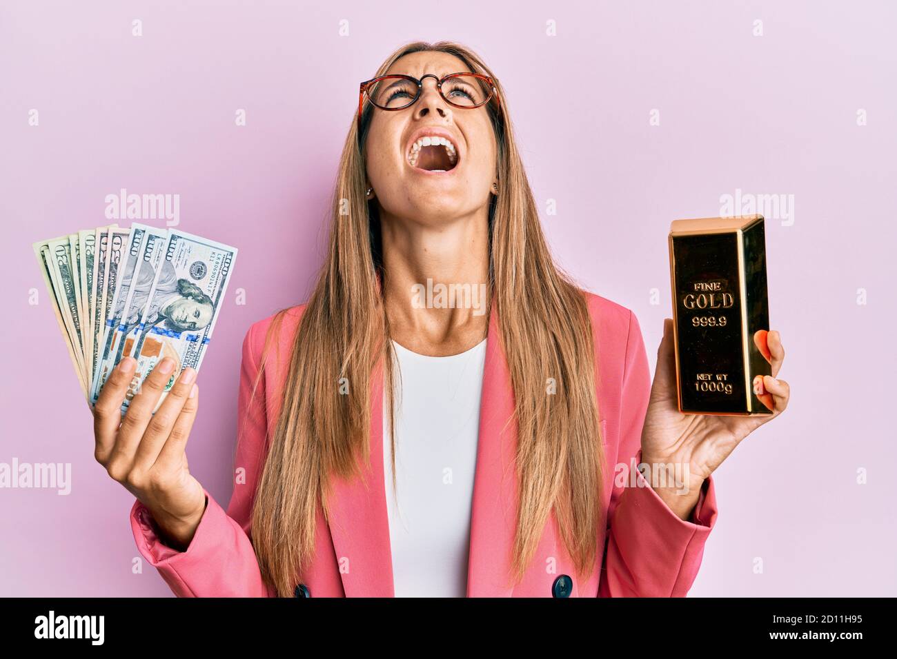 Young blonde woman wearing business style holding gold ingot and ...