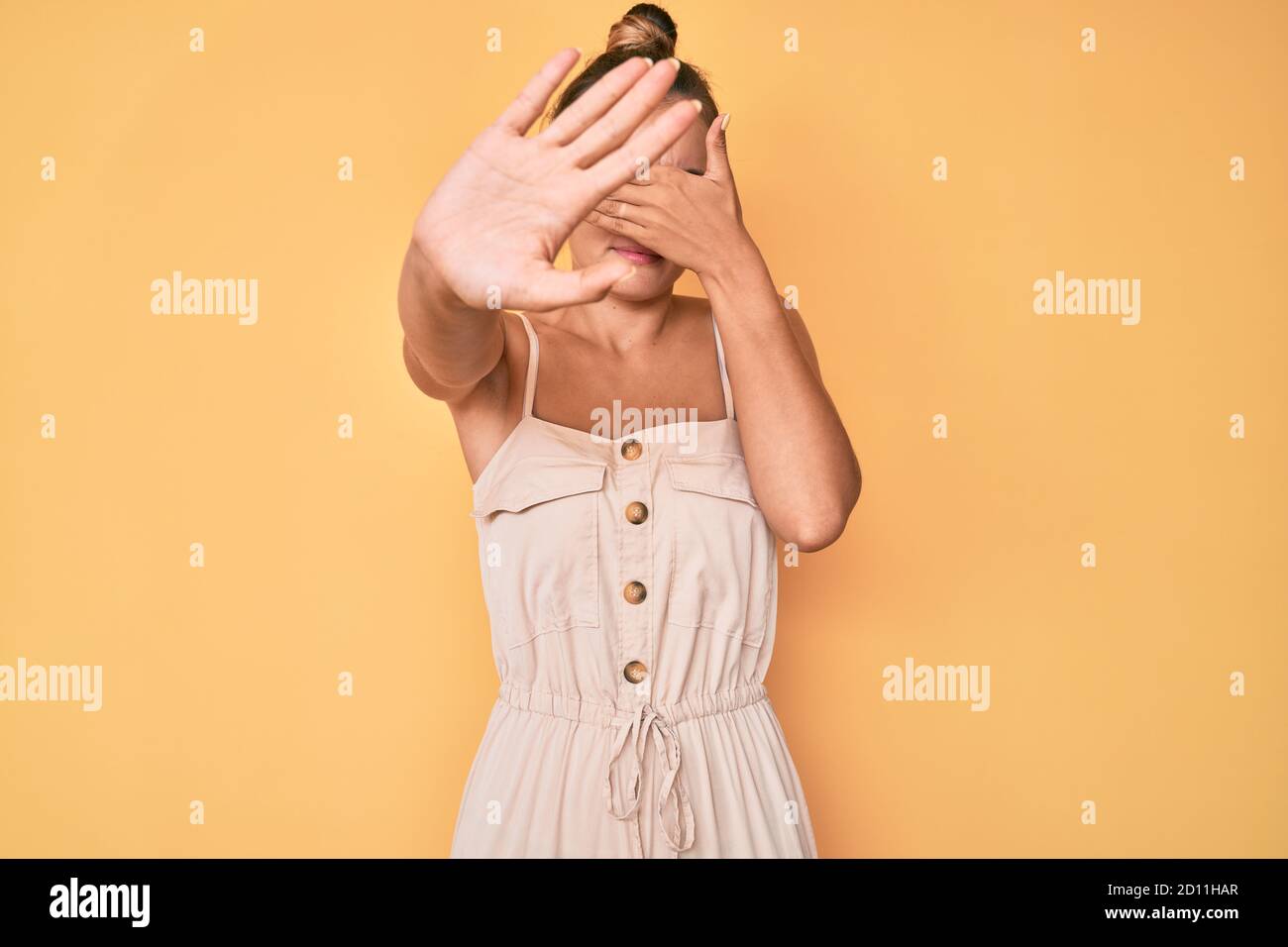 Beautiful caucasian woman wearing summer dress covering eyes with hands ...