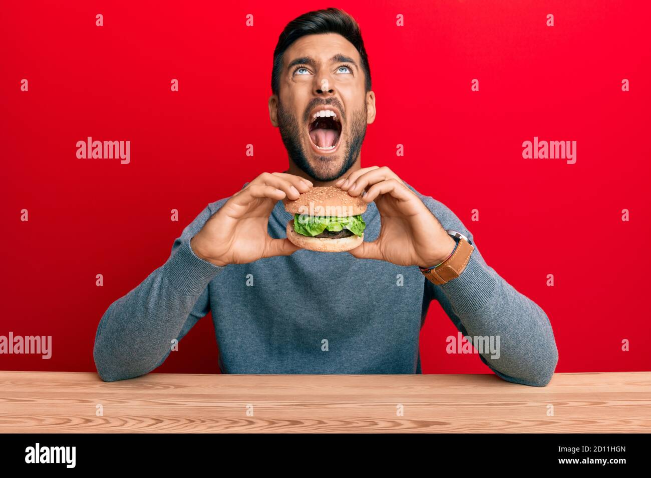 Handsome hispanic man eating a tasty classic burger angry and mad ...