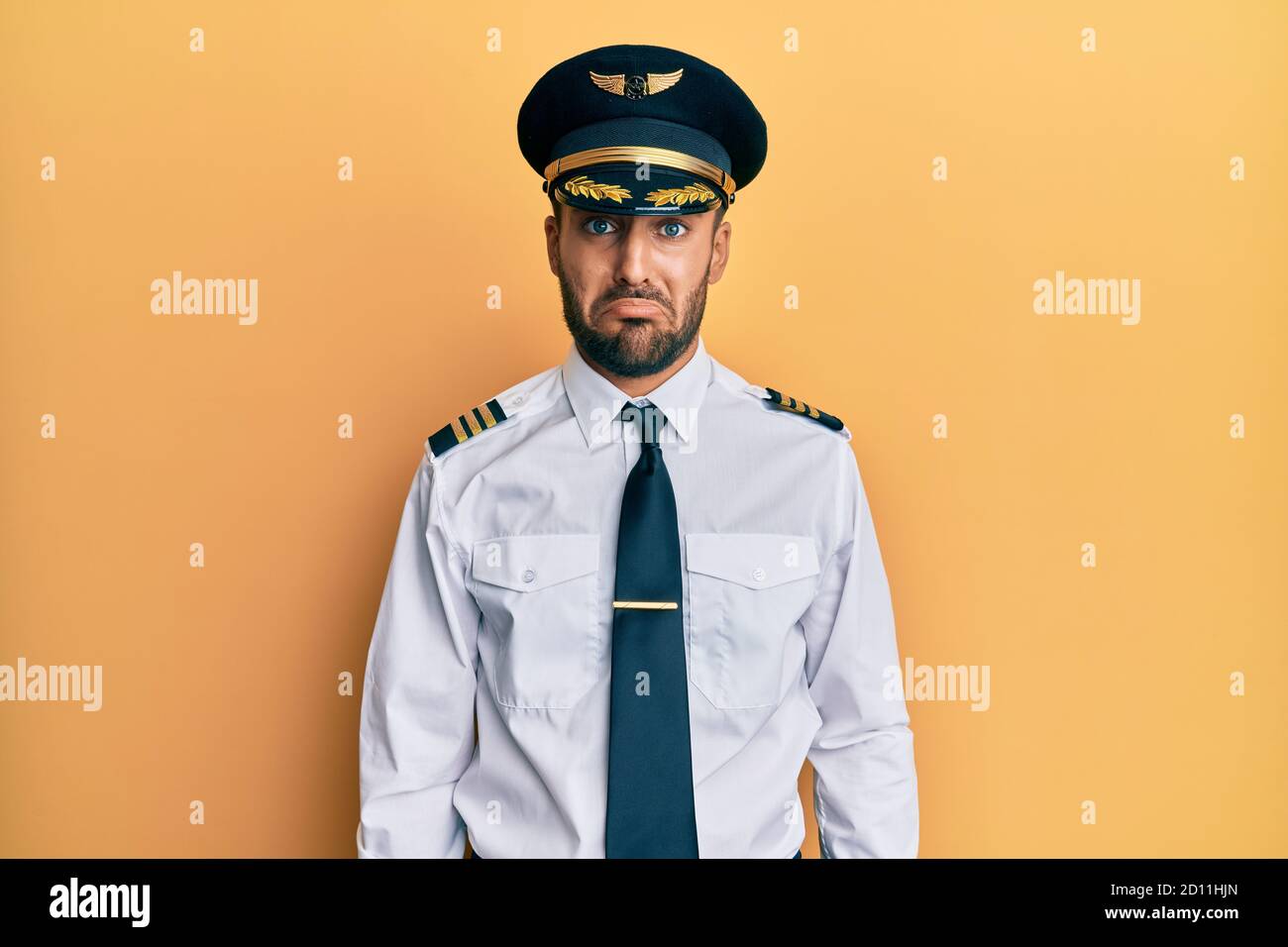 Handsome hispanic man wearing airplane pilot uniform depressed and ...
