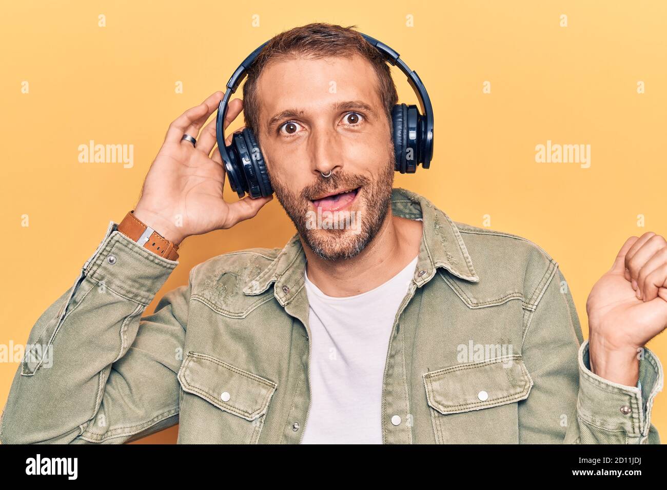Young handsome man listening to music using headphones screaming proud ...