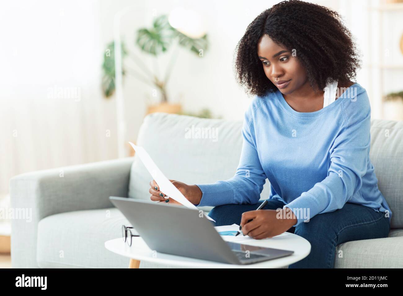Black woman writing report working on laptop at home Stock Photo - Alamy